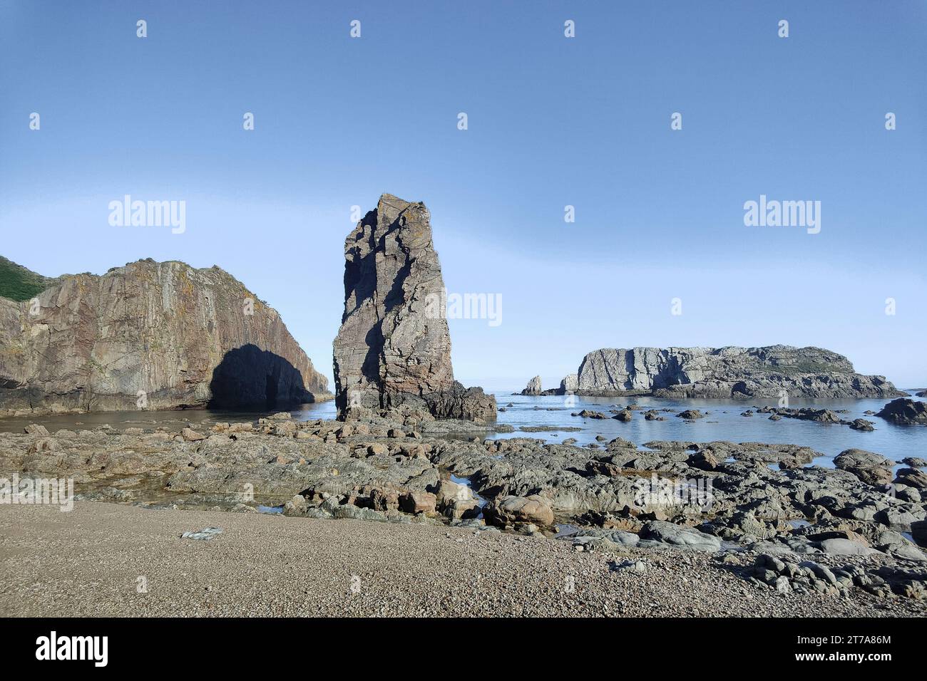 rocky beach with a tall, dark basalt formation in the center ...