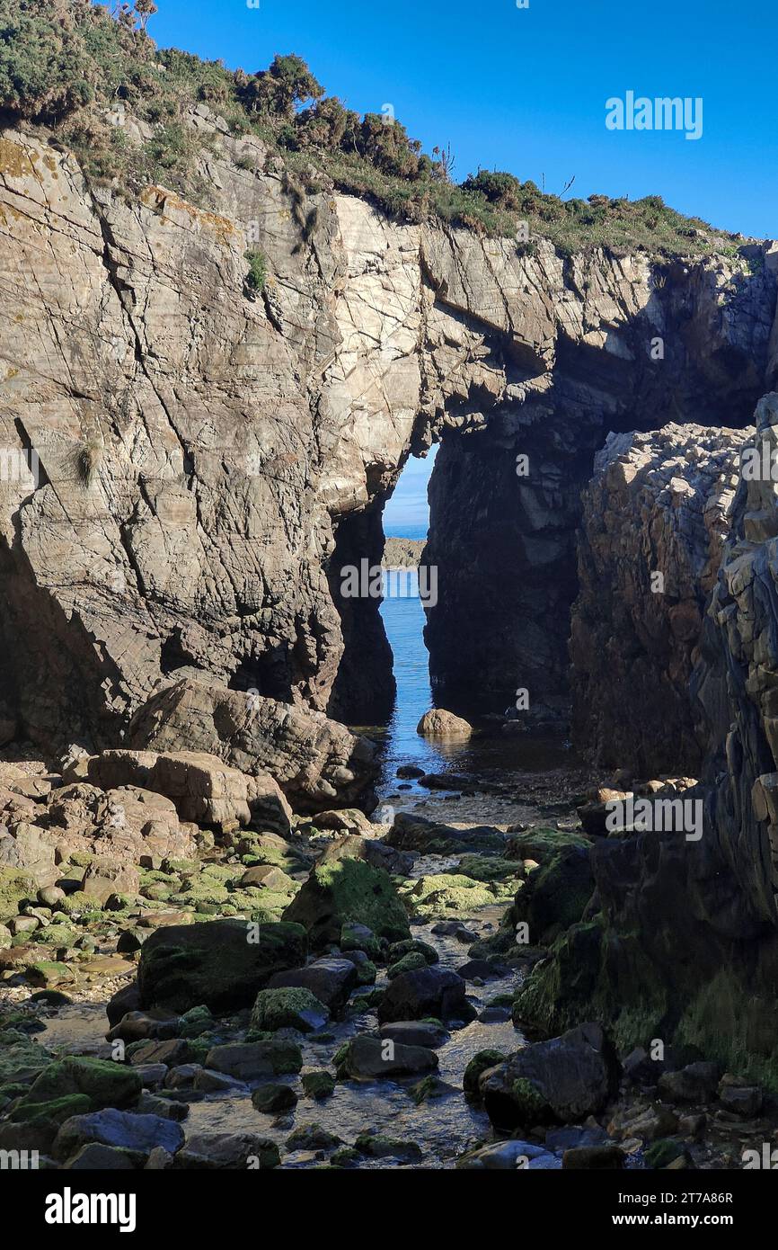 rocky beach features a tall, jagged arch formation, with the deep blue ...
