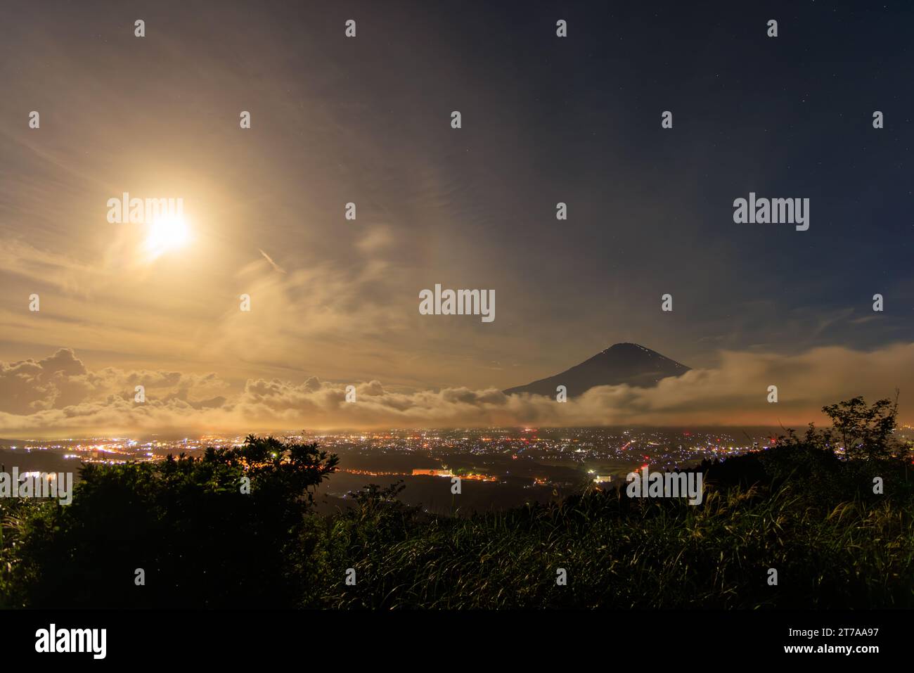 Bright full moon lights clouds over city at base of Mt. Fuji at night ...