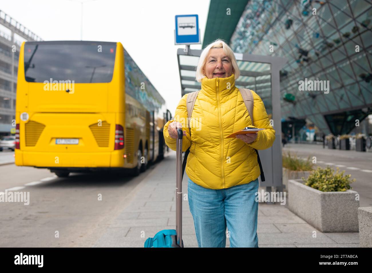 Happy senior woman traveler in a stylish yellow jacket and jeans with a ...