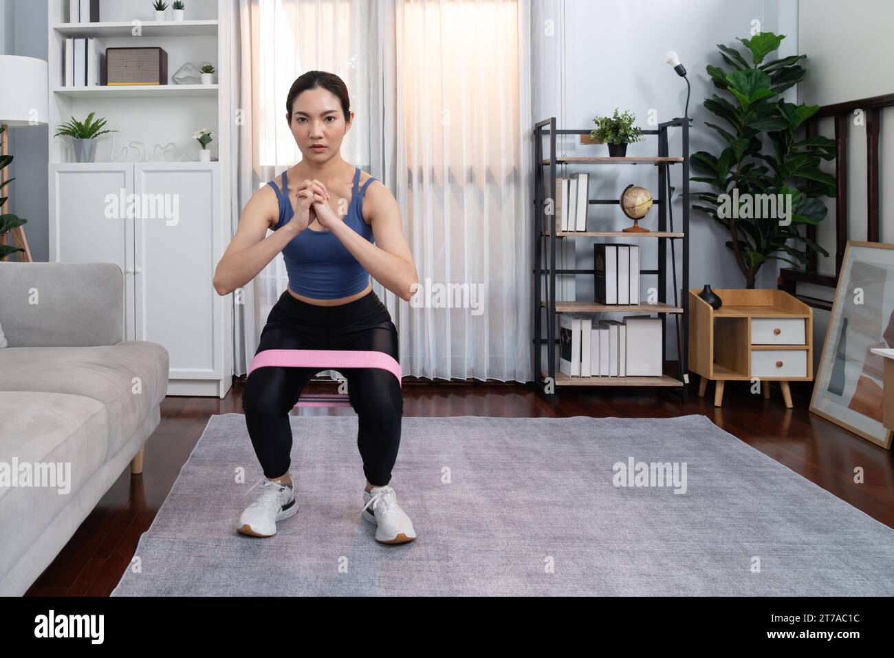 Vigorous energetic woman doing exercise at home with resistance sport ...