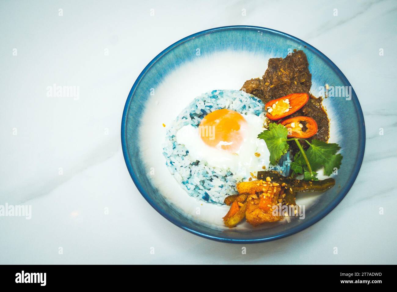 a bowl of beef rendang rice with beef rendang cuves, butterfly pea rice ...