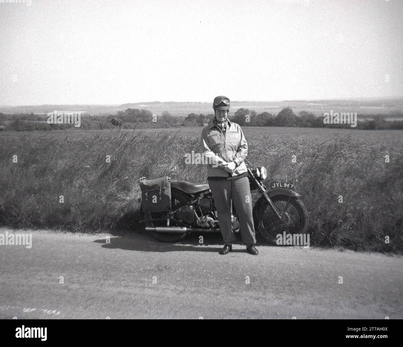 1950s, historical, a male touring motorcyclist stands on a road with ...