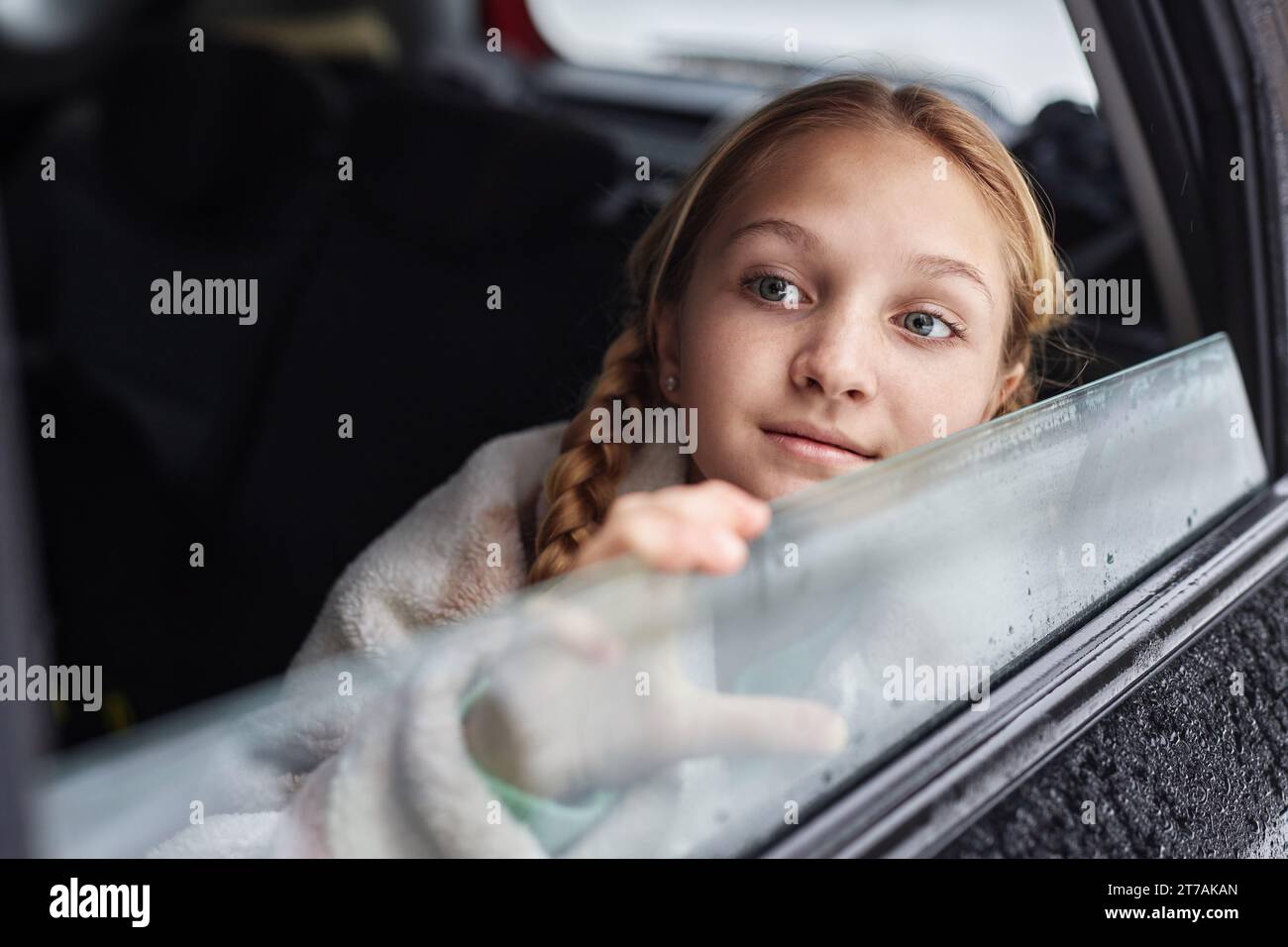 Cute pre-teen girl with pigtails looking forwards from car window while ...