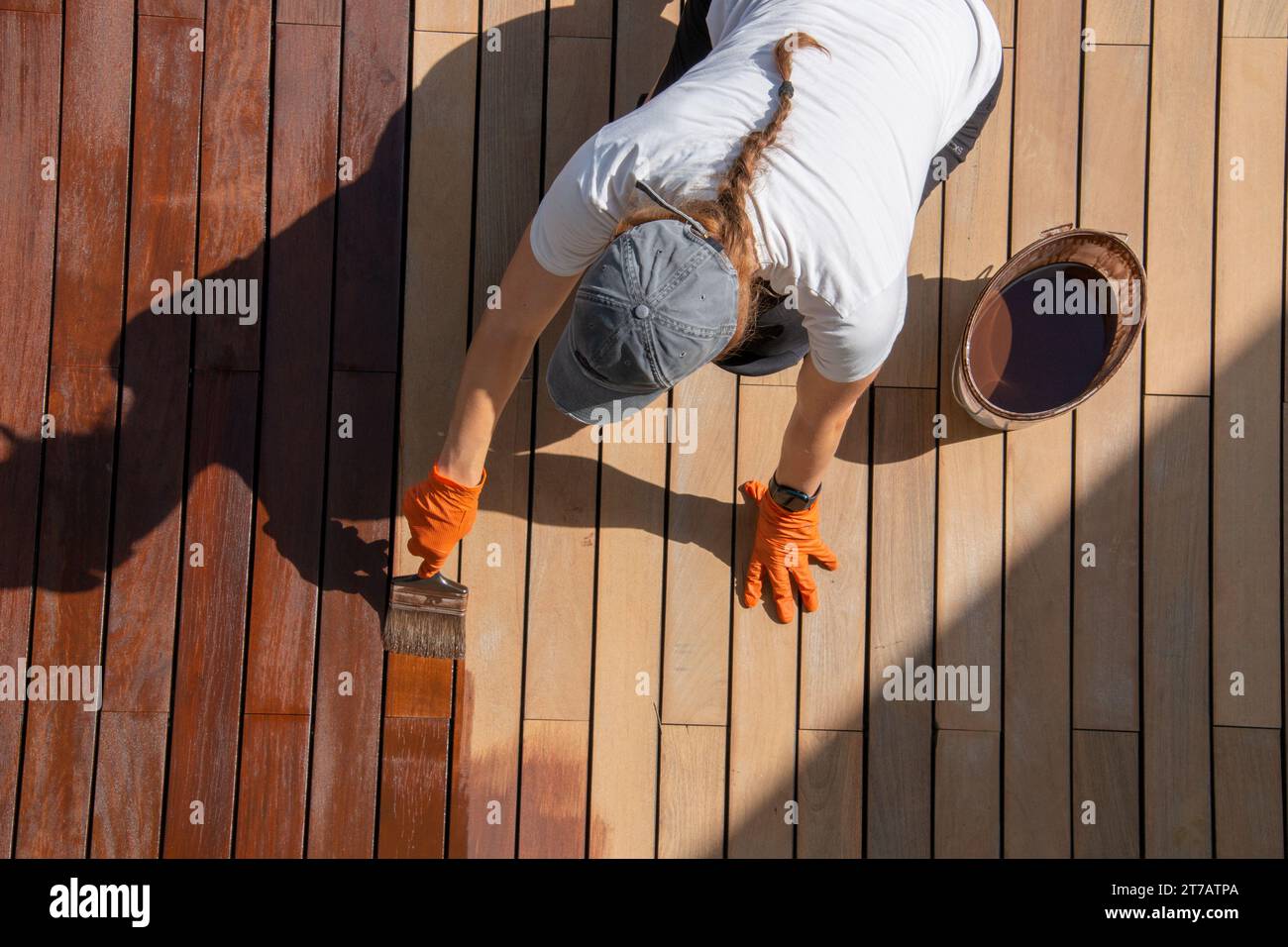 Workwoman staining wood deck boards outdoors, half body overhead view ...
