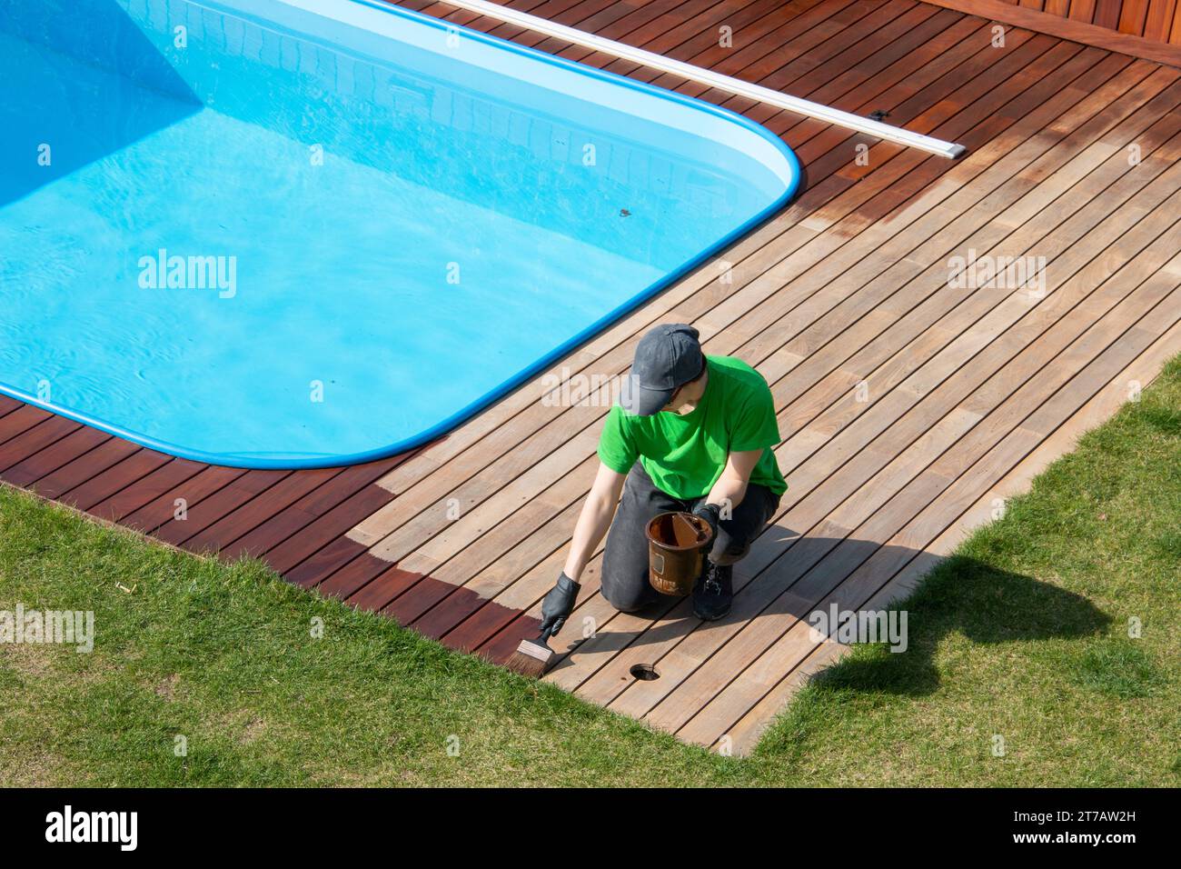 A worker painting exterior wooden pool deck with decking oil Stock ...