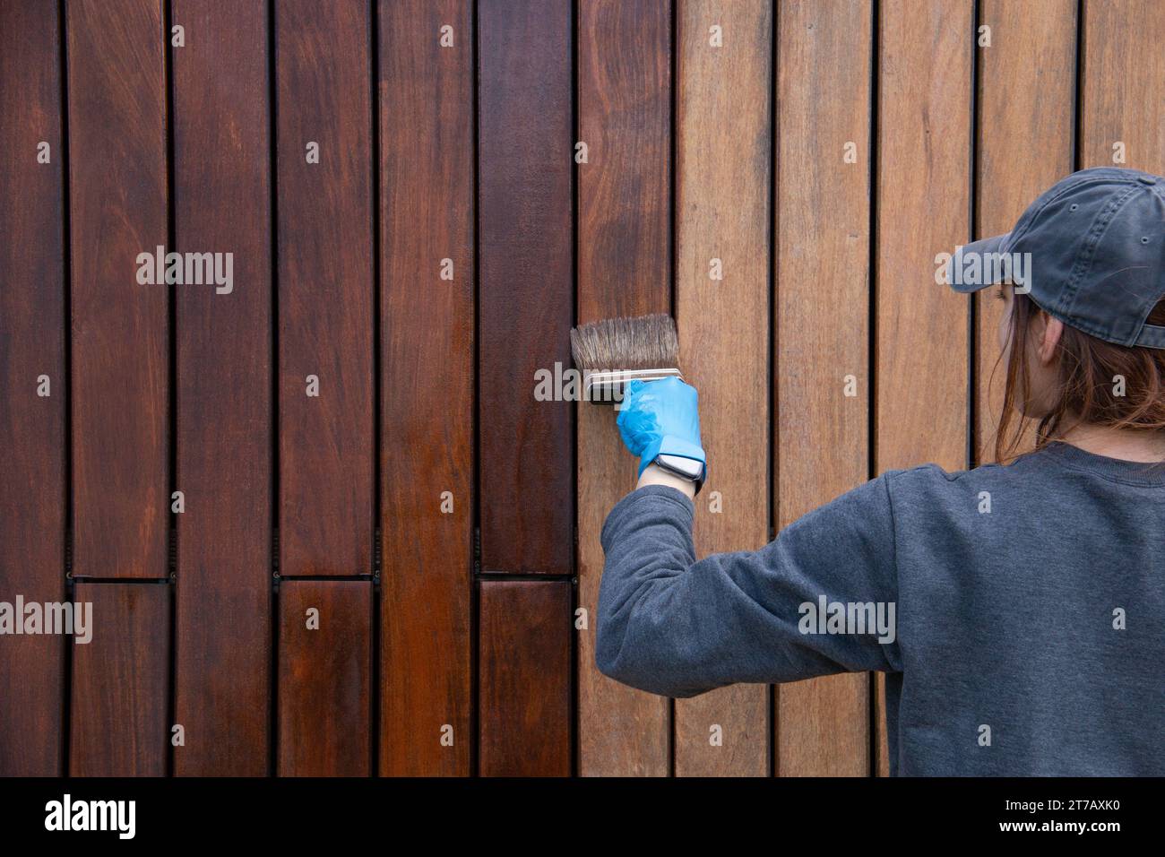 Handywoman applying protective varnish or paint with brush on wood ...