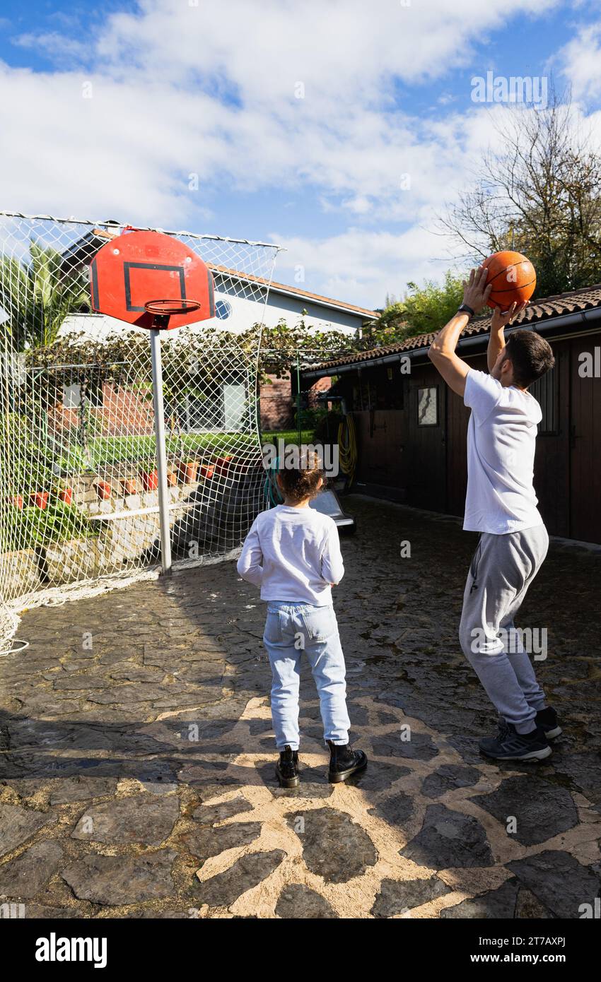 Father playing basketball with his daughter, throwing a shot to put it ...