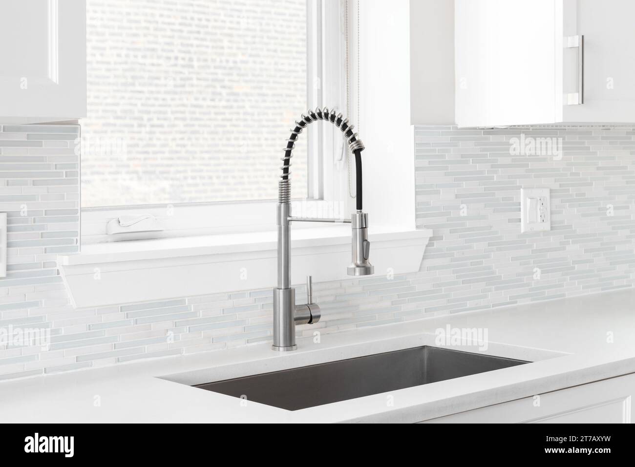 A kitchen faucet detail with a polished stainless steel faucet, a glass ...