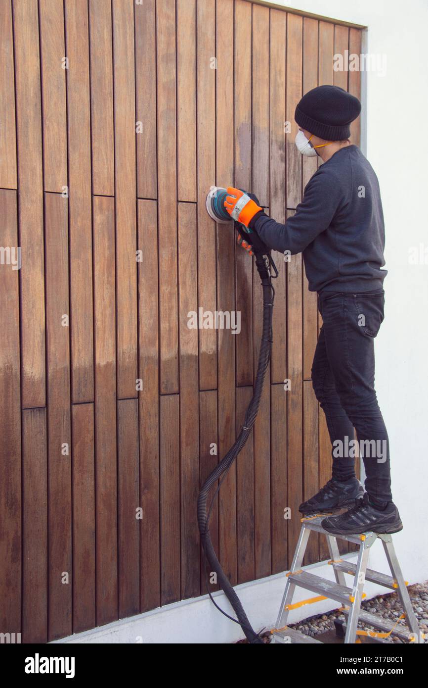 Man in dust mask sanding teak cladding on the house facade, exterior ...