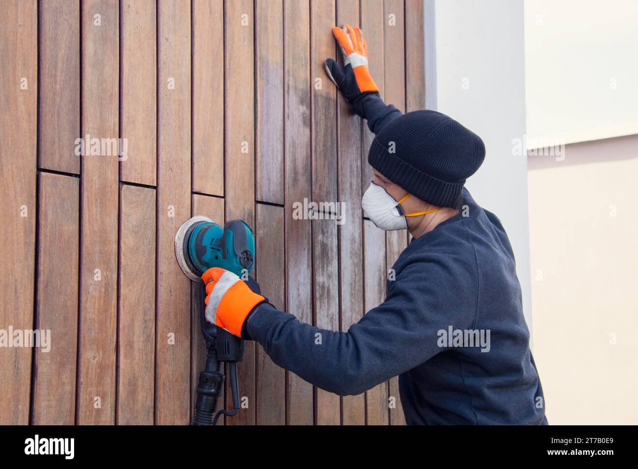 Man in dust mask sanding teak cladding on the house facade, exterior ...