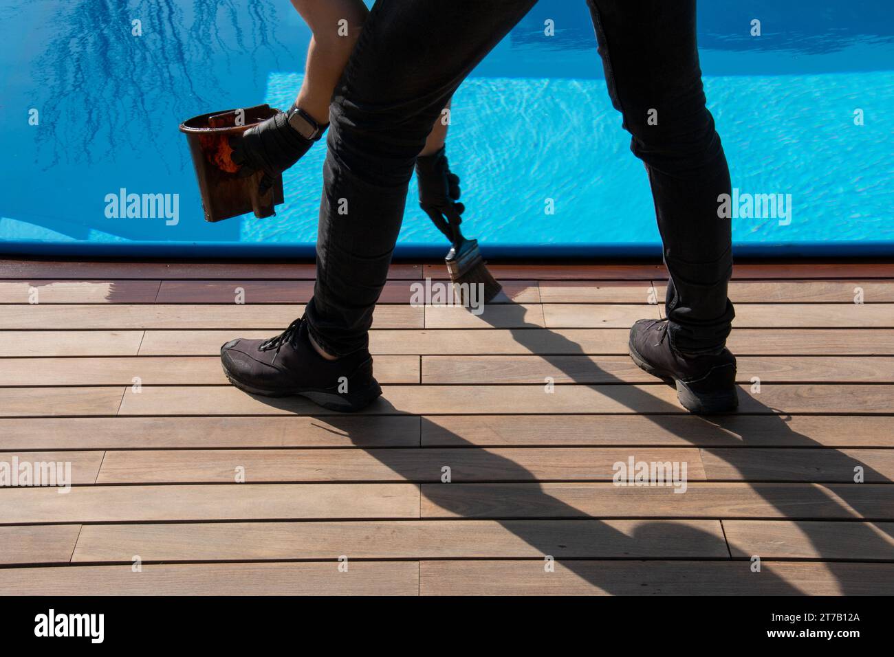 Pool deck terrace renovation. Person applying brown wood protection oil ...
