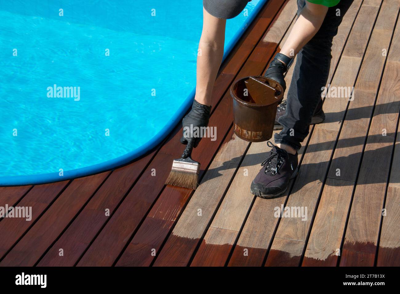 Worker applying brown wood protection oil on decking boards with paint ...