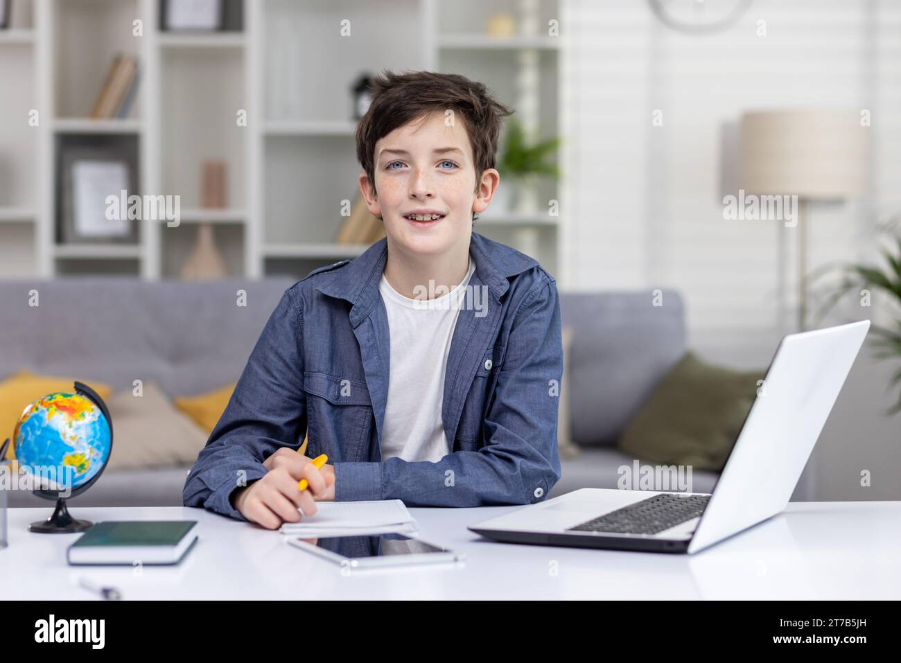 Portrait of happy teenage boy student sitting at table at home ...