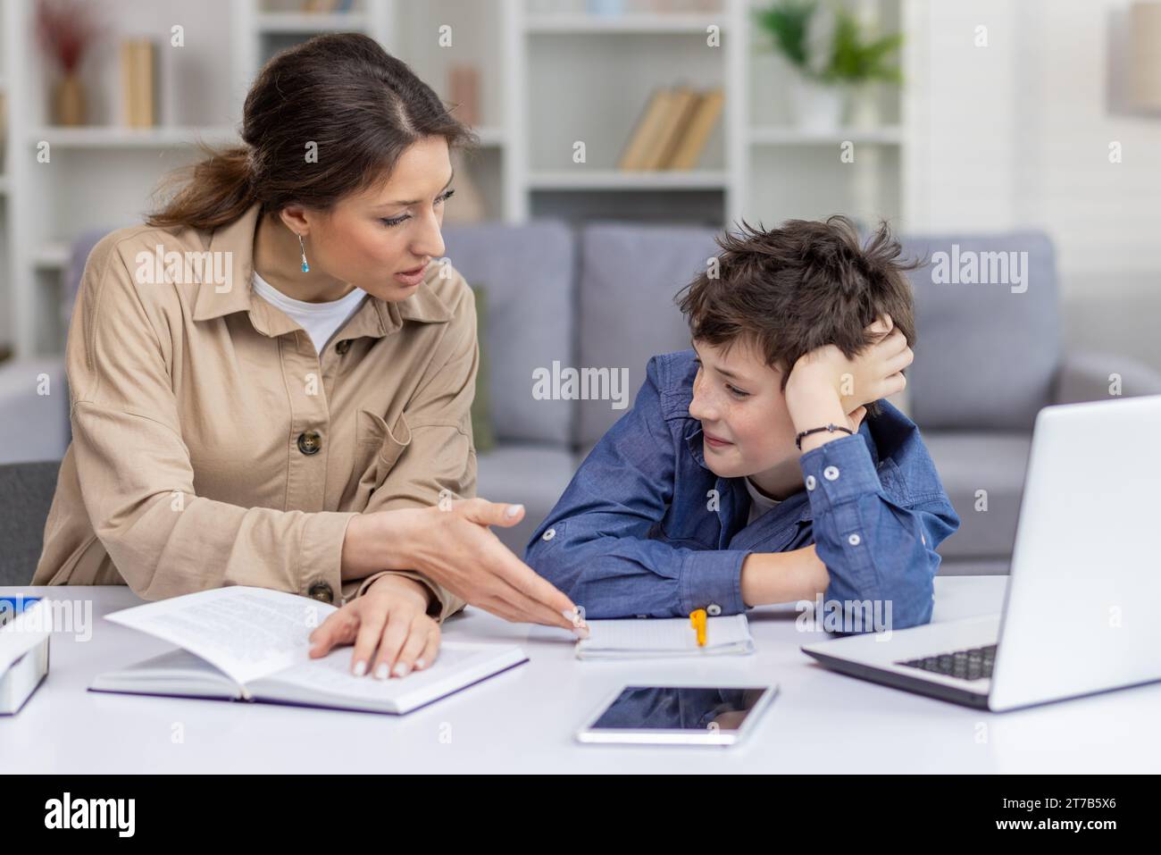 A female tutor works with a boy student in a bright living room at home ...