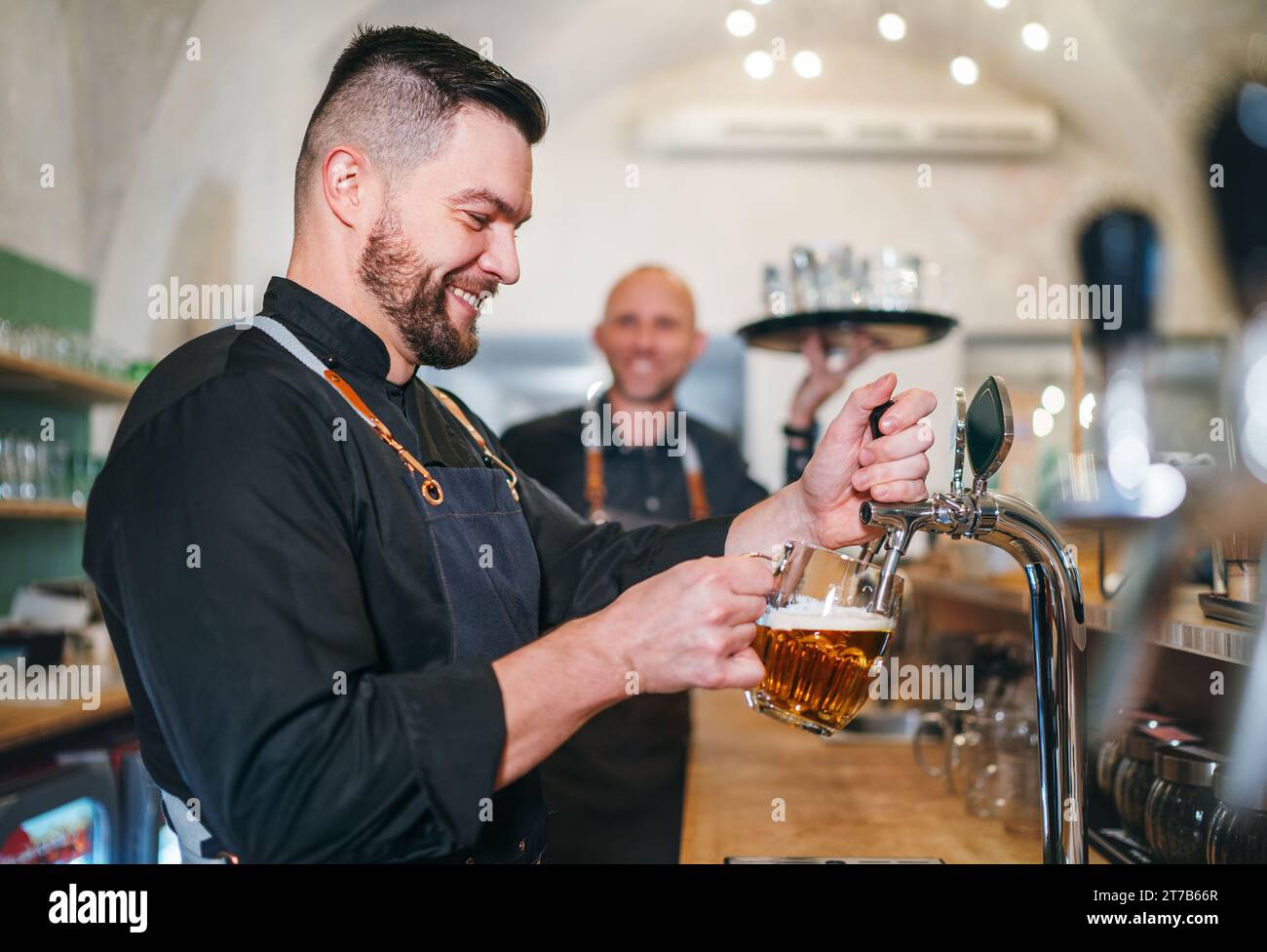 Stylish bearded barman dressed black uniform beer tapping at bar ...