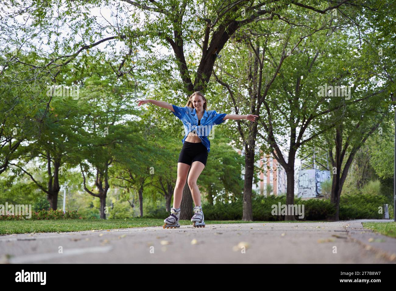 young woman skating on inline skates in the park with open arms ...