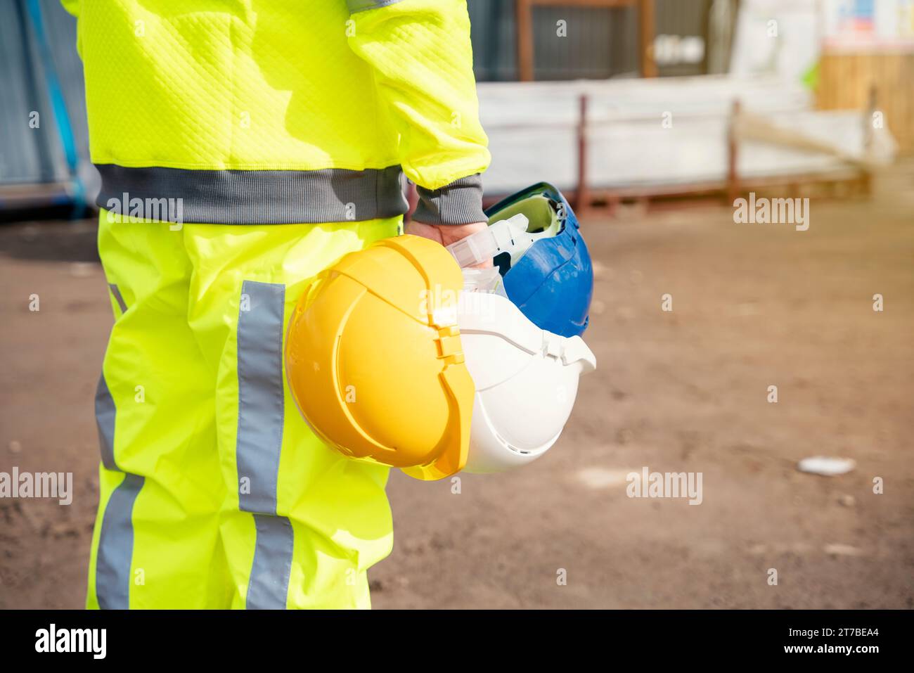 Builder wearing hi-viz reflective suit with three helmets in hand ...