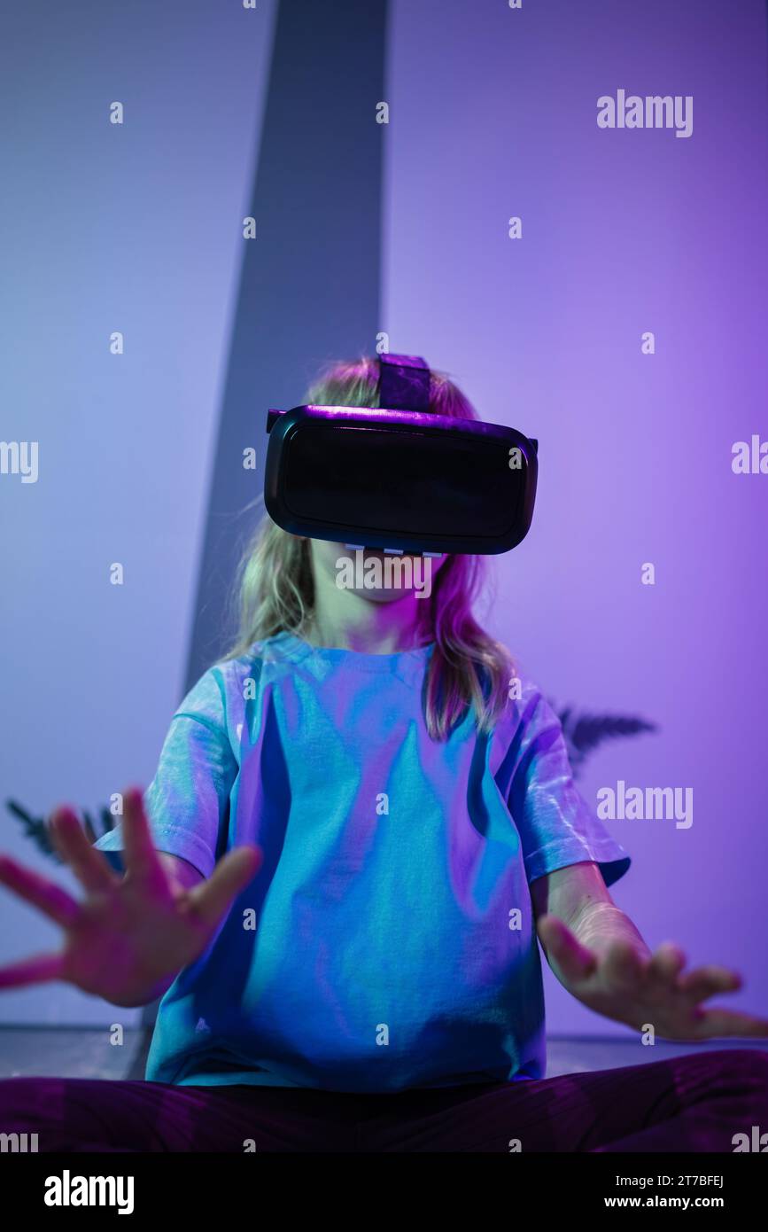School aged girl child in VR glasses sitting on the floor, having an ...