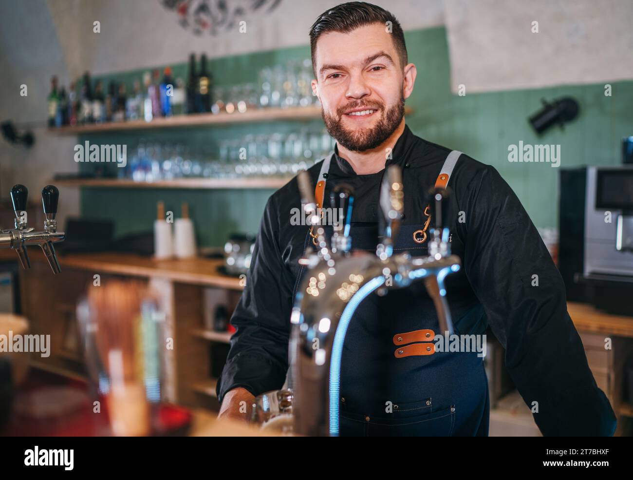 Portrait of happy smiling bearded barman dressed in a black uniform ...