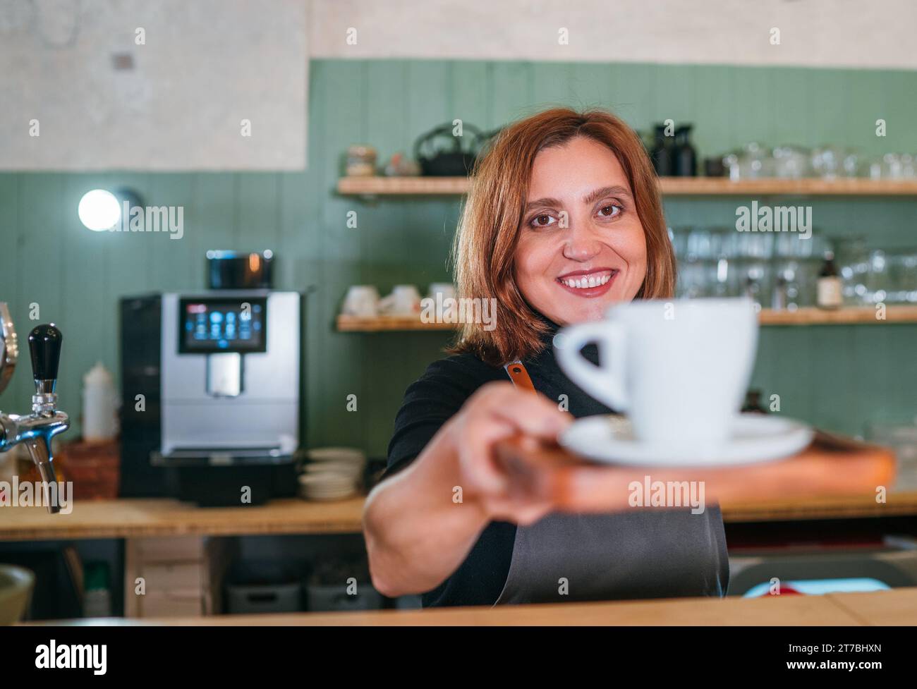 Cheerfully smiling barista female giving white cup aromatic espresso at ...
