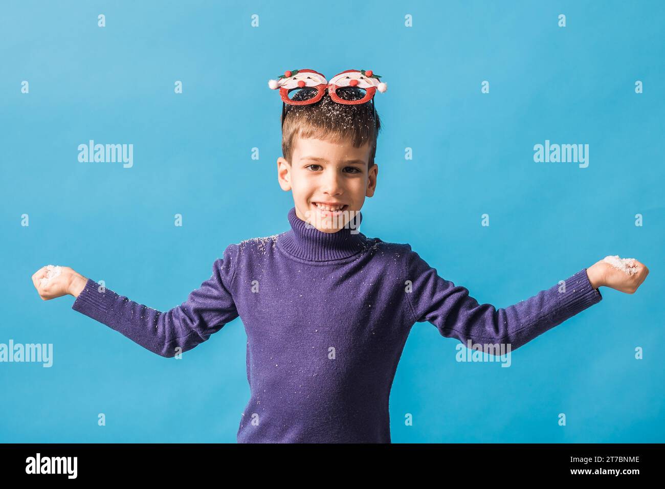 Child boy throws up snow on blue background. Christmas and New Year holidays concept. Generation ...