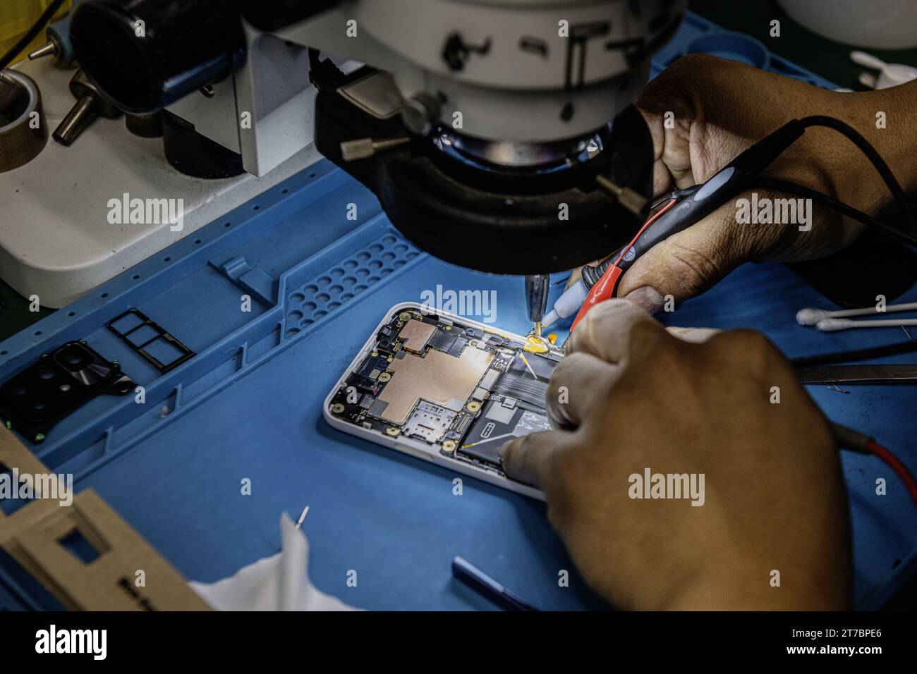 A technician repairing a mobile phone under a magnifying microscope on ...