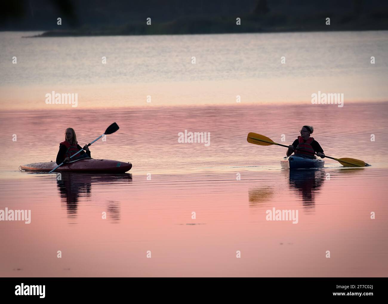 Silhouette of 2 Kayakers paddling at sunset during golden hour lake ...