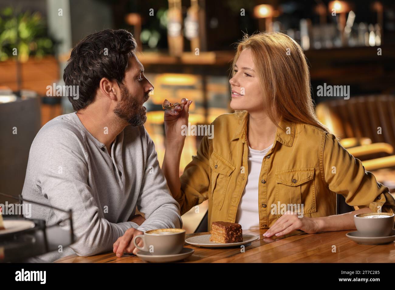 Romantic date. Beautiful woman feeding her boyfriend with cake in cafe ...