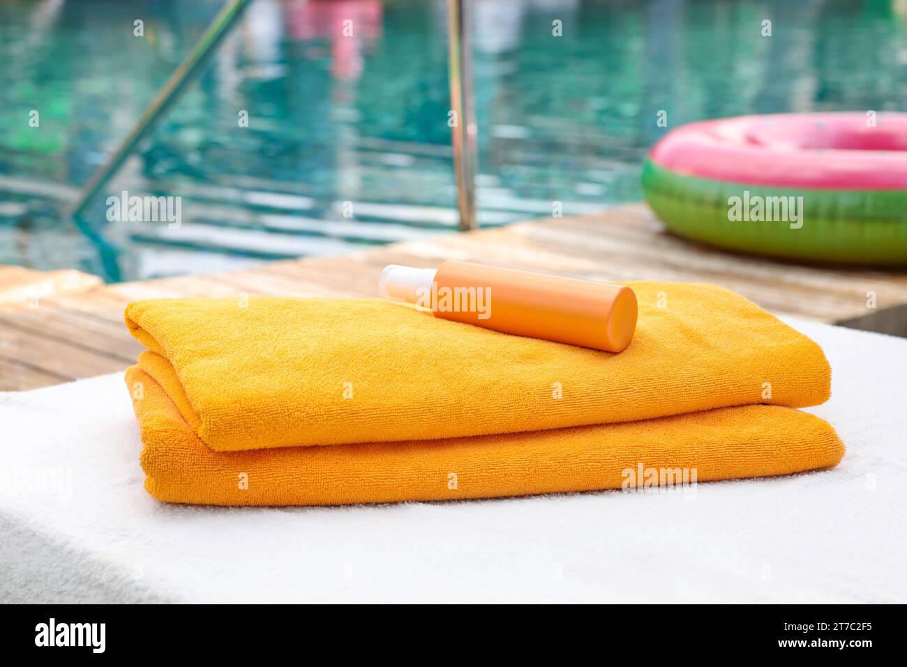 Beach towels and sunscreen on sun lounger near outdoor swimming pool ...