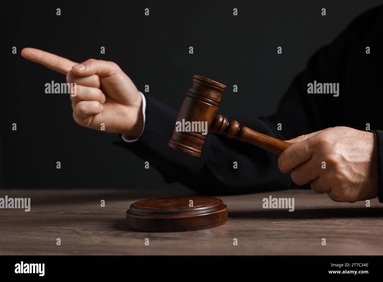 Judge with gavel pointing at wooden table against black background ...