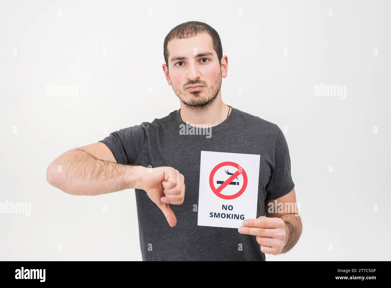 Young man holding no smoking sign showing thumbs down against white ...
