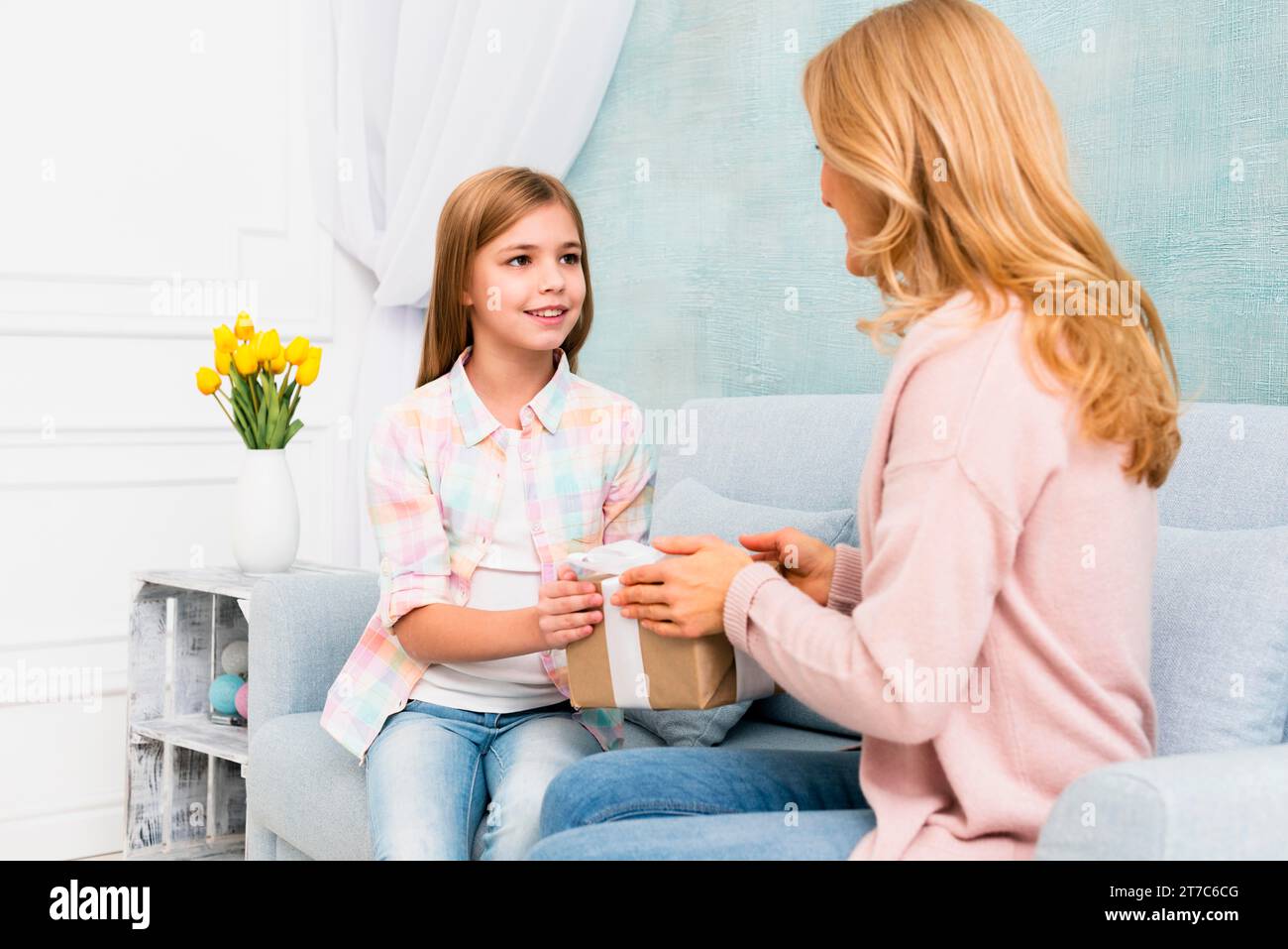 Daughter giving gift box mom sitting couch Stock Photo - Alamy