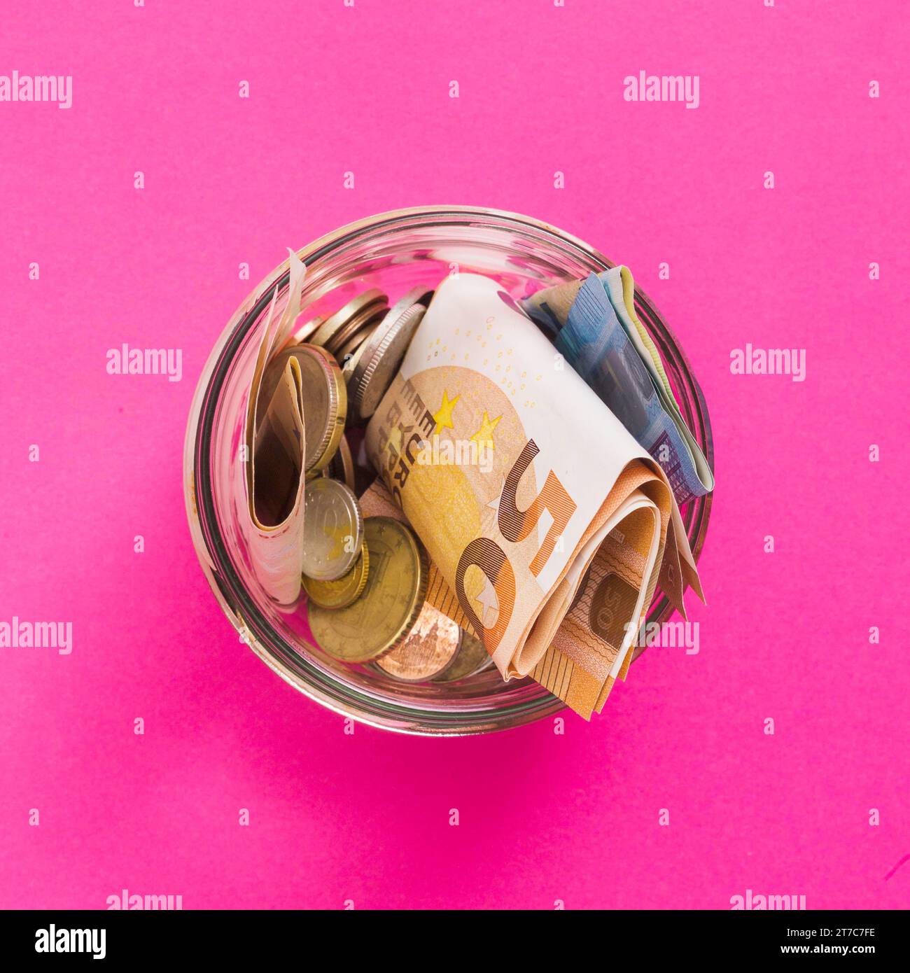 Overhead view euro banknotes coins open glass jar against pink ...