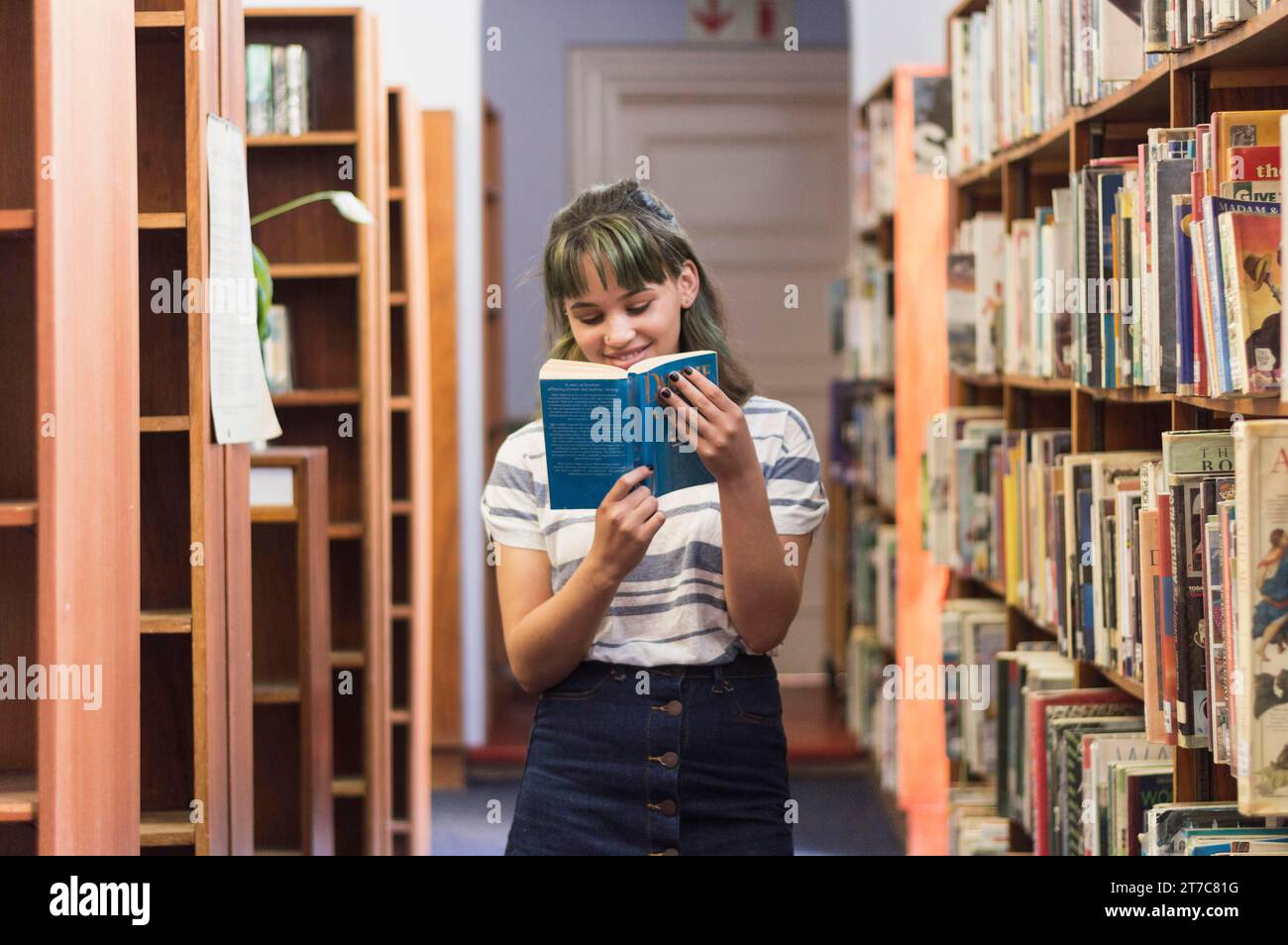 Smiling schoolgirl reading book library Stock Photo - Alamy