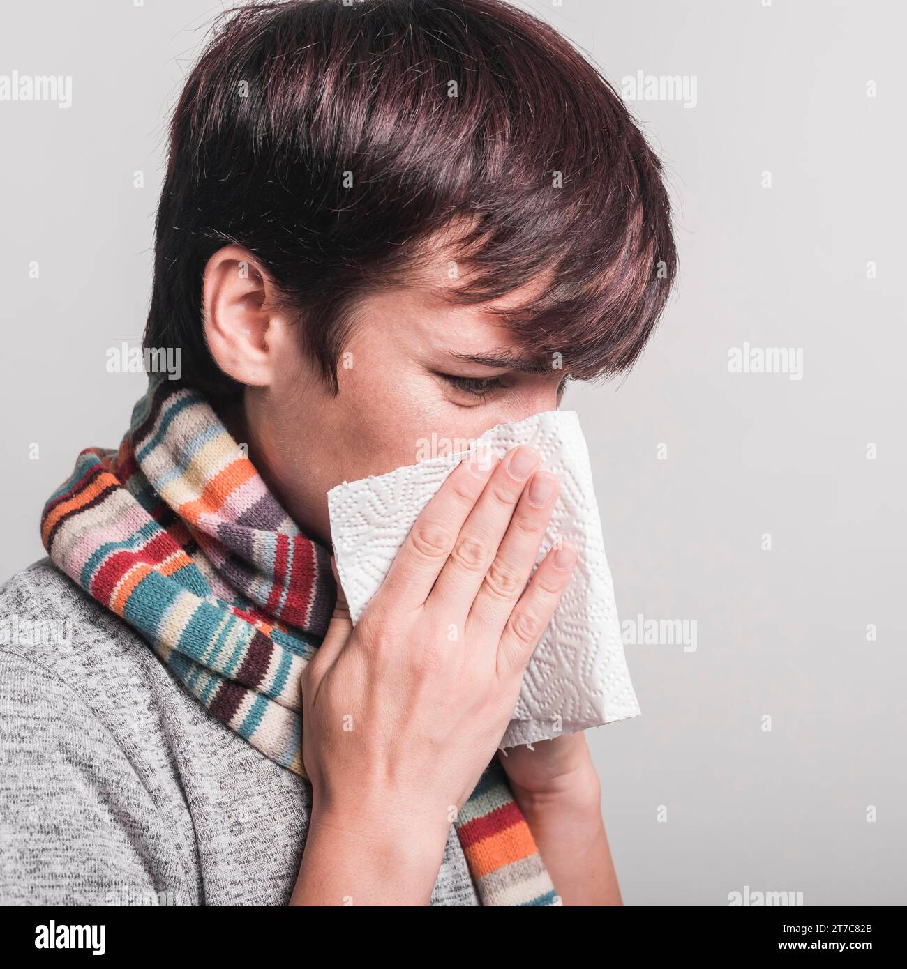 Sick woman blowing nose tissue paper against gray background Stock ...