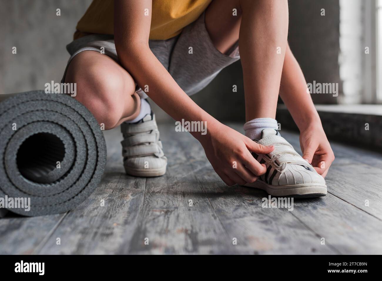 Low section boy putting his shoe strap near rolled up exercise mat ...