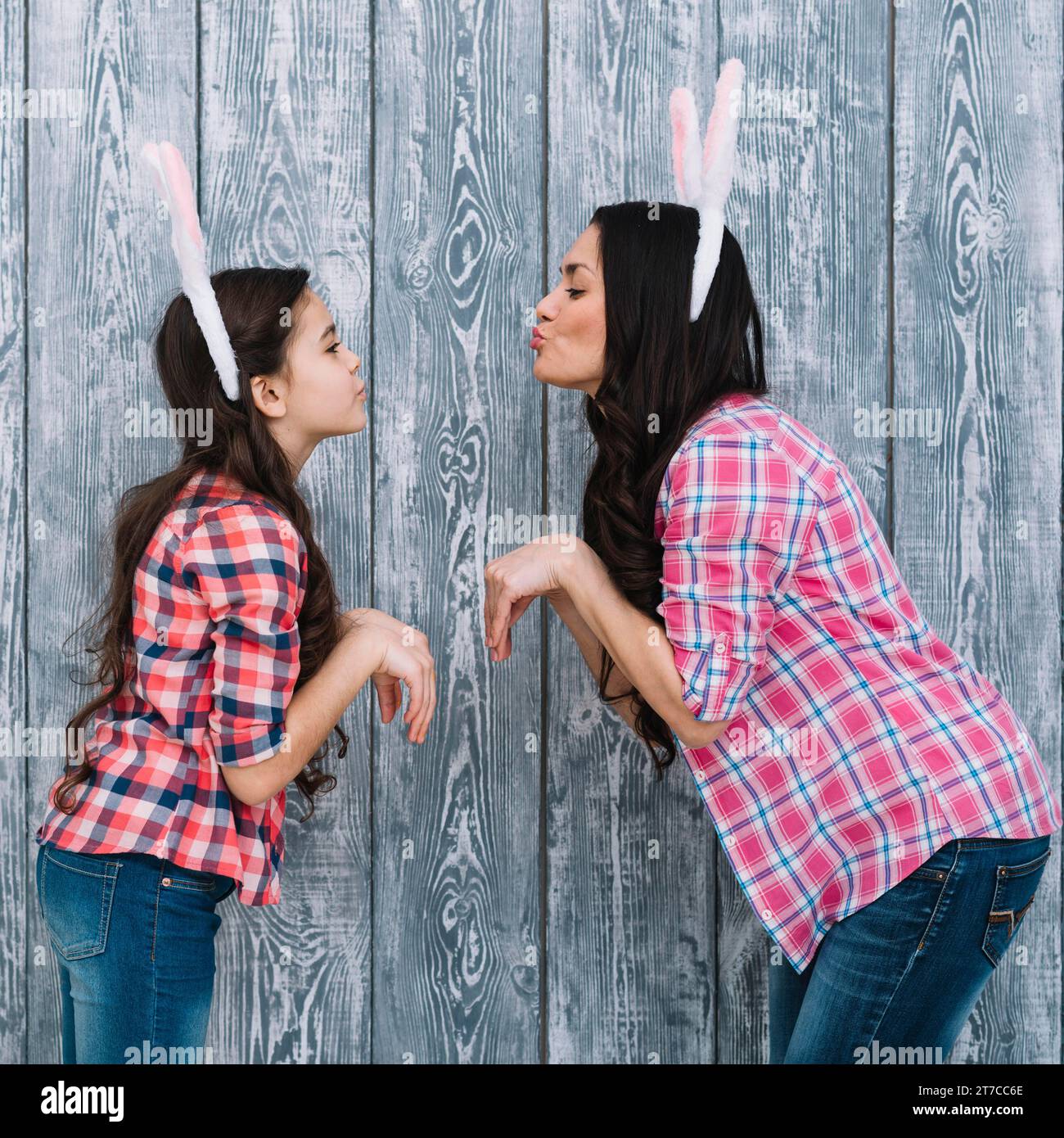Side view daughter mother posing like bunny pouting against gray wooden ...