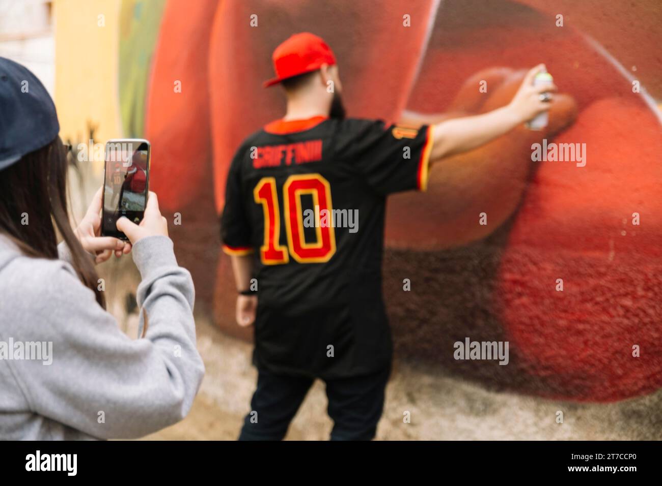 Woman taking graph man spraying graffiti wall Stock Photo - Alamy