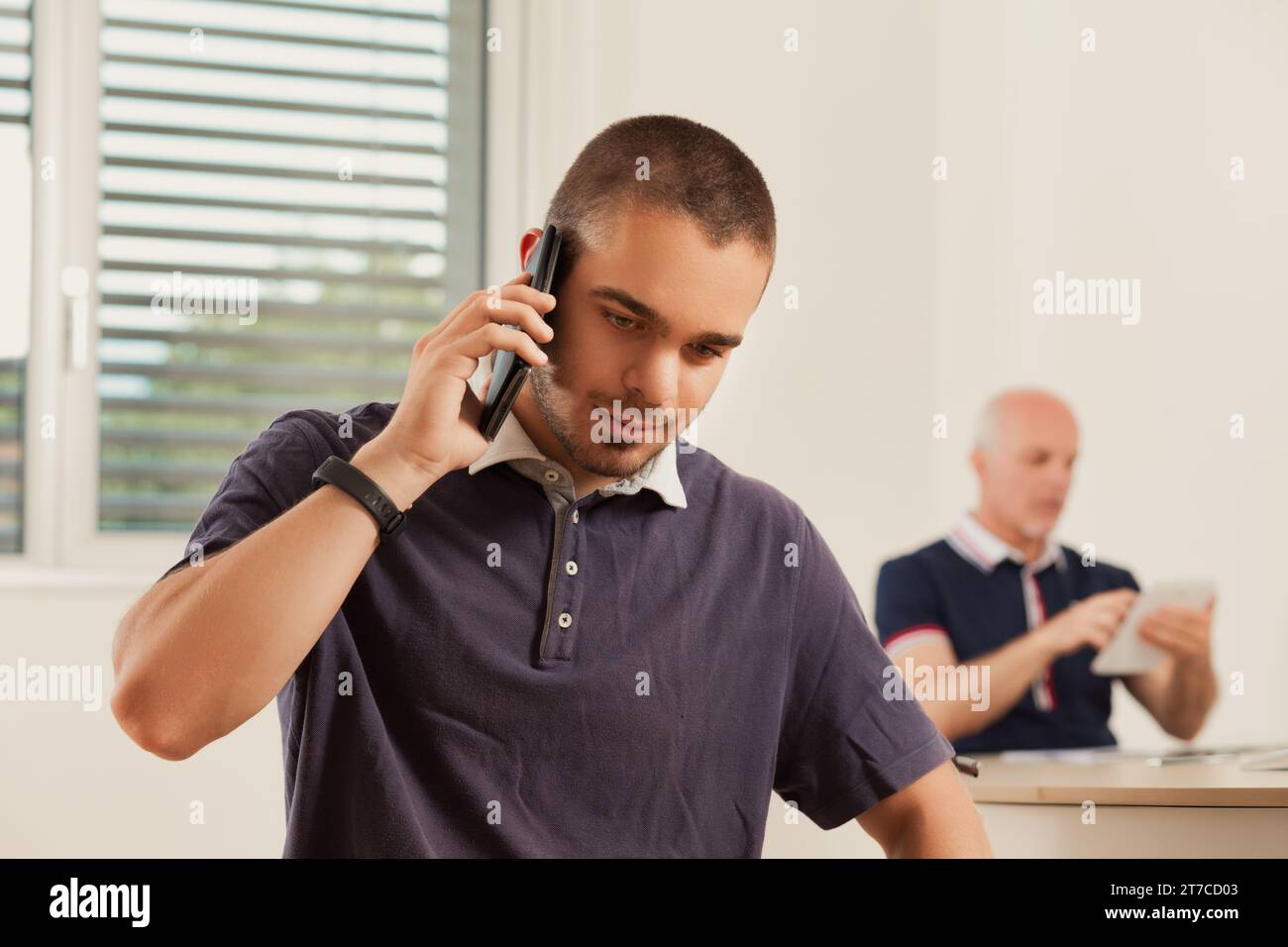Office scene where a young professional takes a call, another person ...