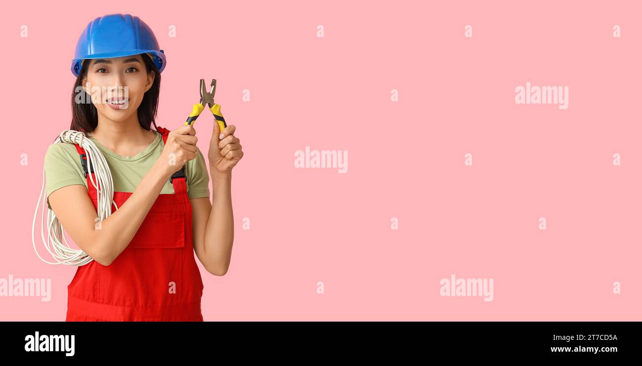 Asian female electrician holding pliers on pink background with space ...