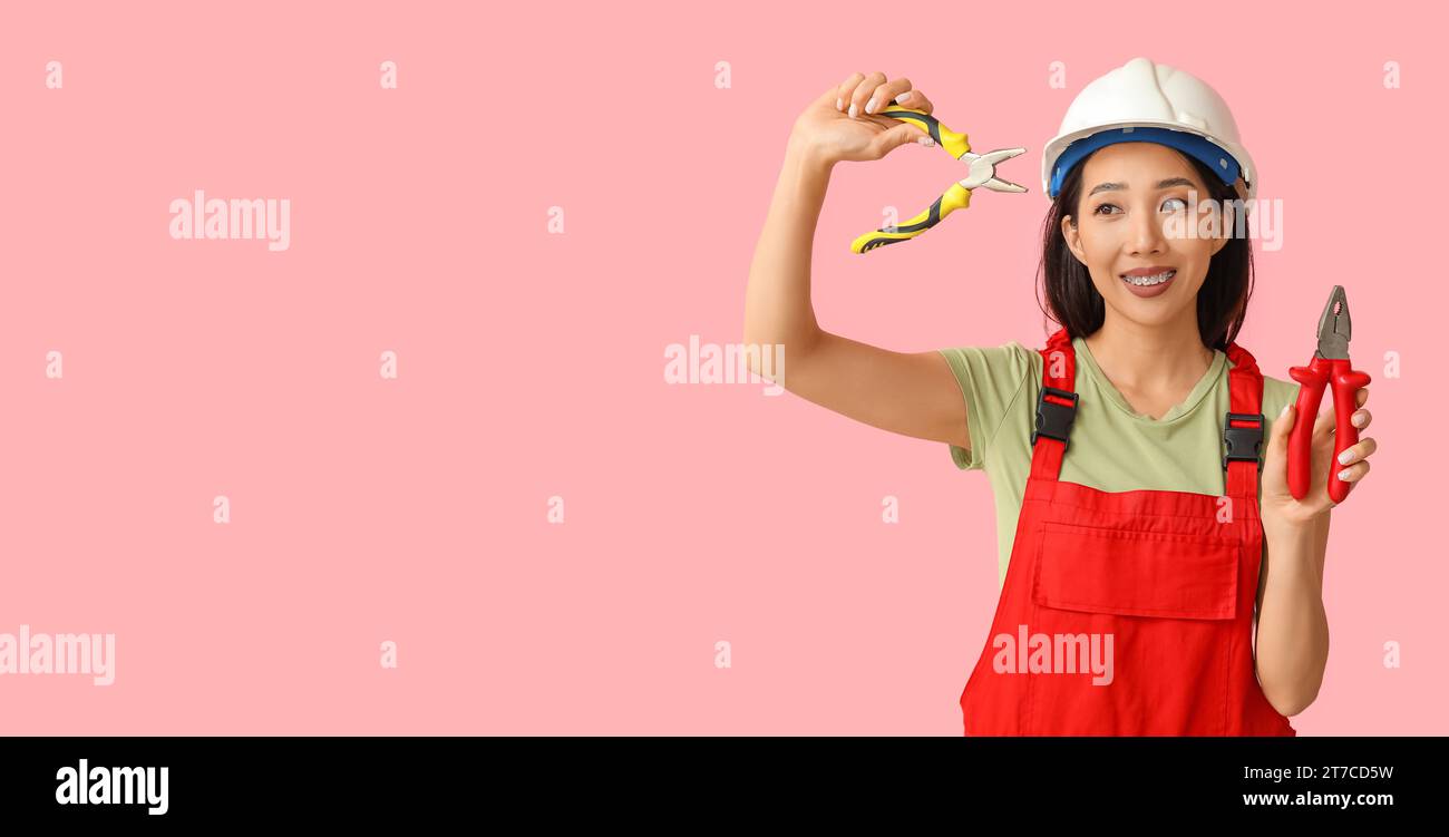 Asian female electrician holding pliers on pink background with space ...