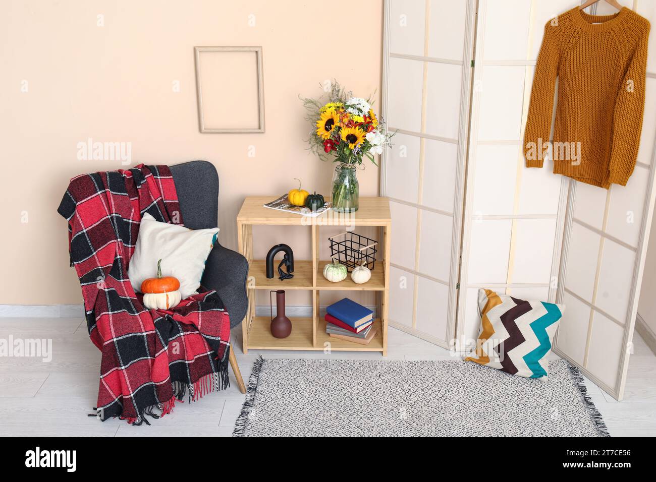 Interior of living room with autumn flowers on shelving unit, armchair ...