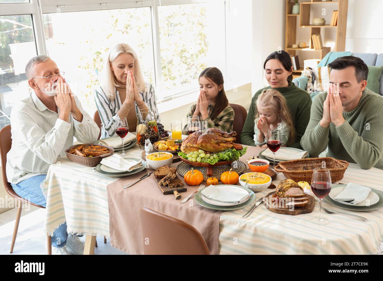 Happy family praying before dinner at festive table on Thanksgiving Day ...