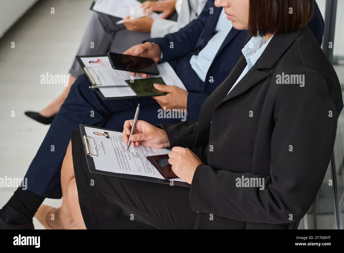 Group of people filling documents to get visa while sitting in queue in ...
