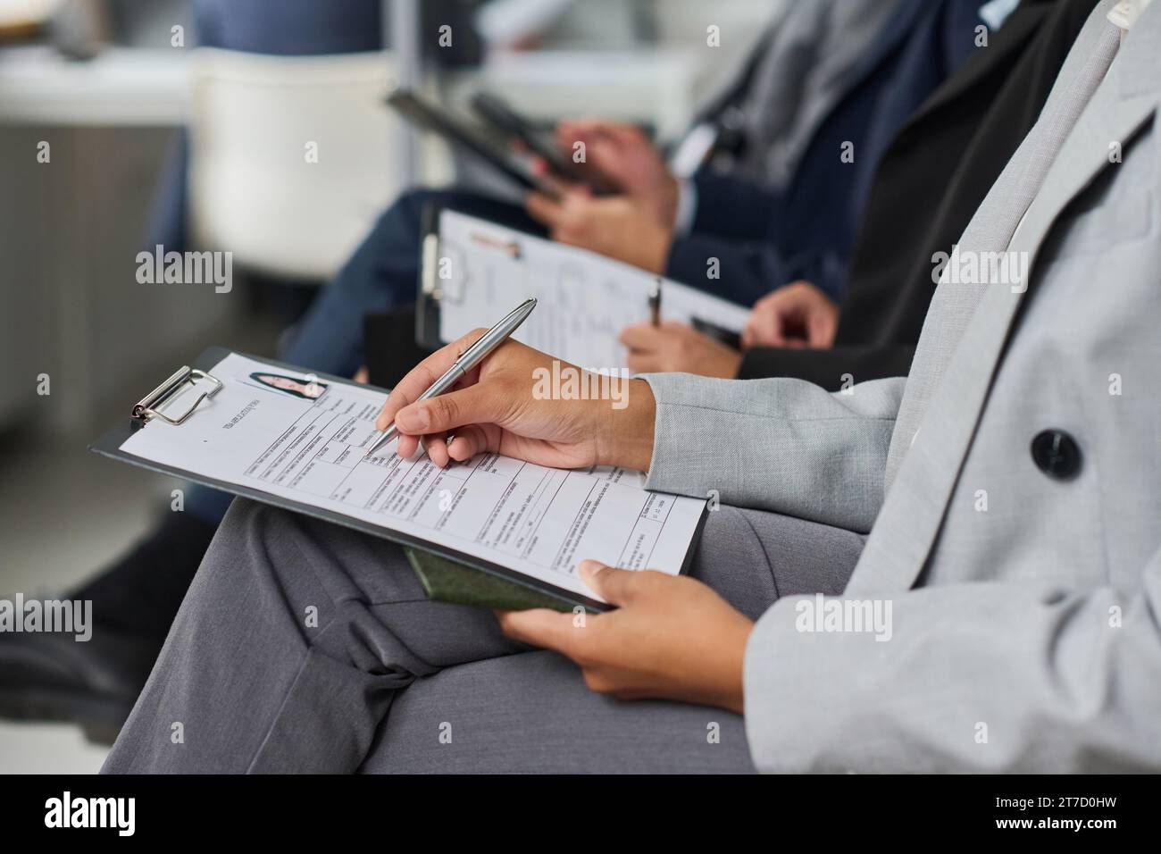 Close-up of people sitting in a row and filling documents for visa ...