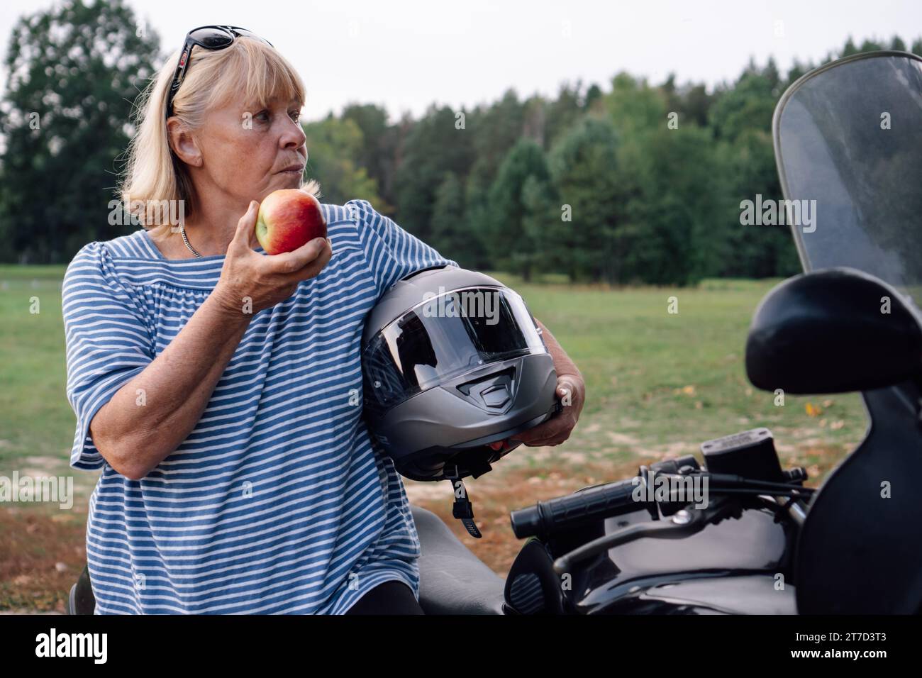 Female biker. Eating apple pretty blonde middle-aged biker near her ...