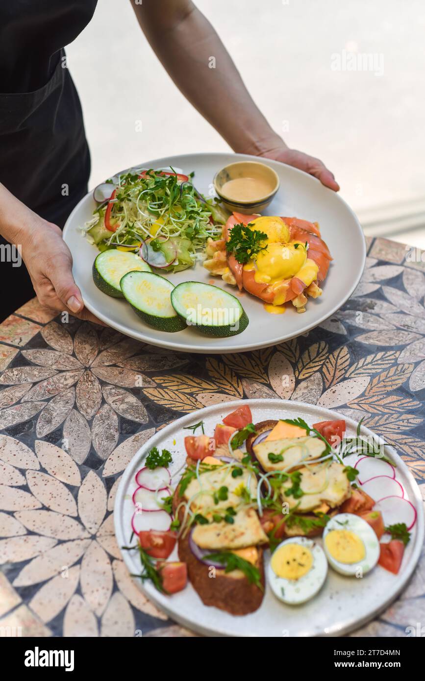waitress holding a plate with eggs bennedict waffles with smoked salmon ...