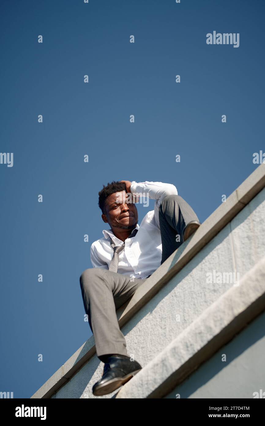 Vertical image of young man in depression sitting on the roof and ...