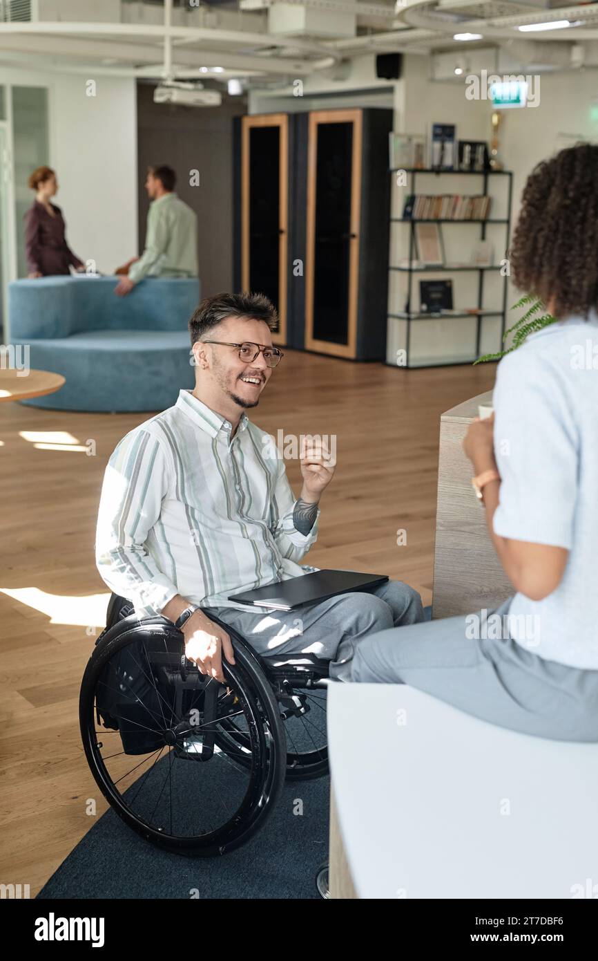 Vertical image of man with disability talking to his colleague while ...